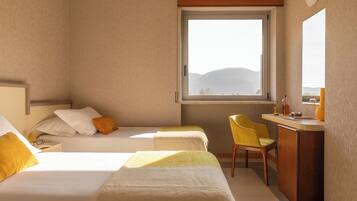 Quarto de hotel com duas camas, uma escrivaninha, uma cadeira, janela com vista e um espelho.