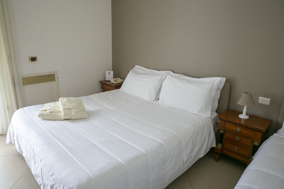 Quarto de hotel com uma cama grande, uma mesa de cabeceira com abajur e um telefone.