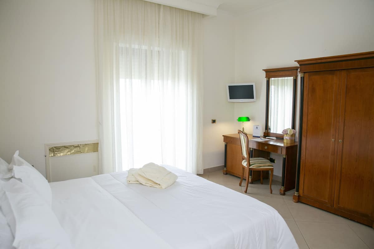 Quarto de hotel com cama, escrivaninha, cadeira, televisão e guarda-roupa.
