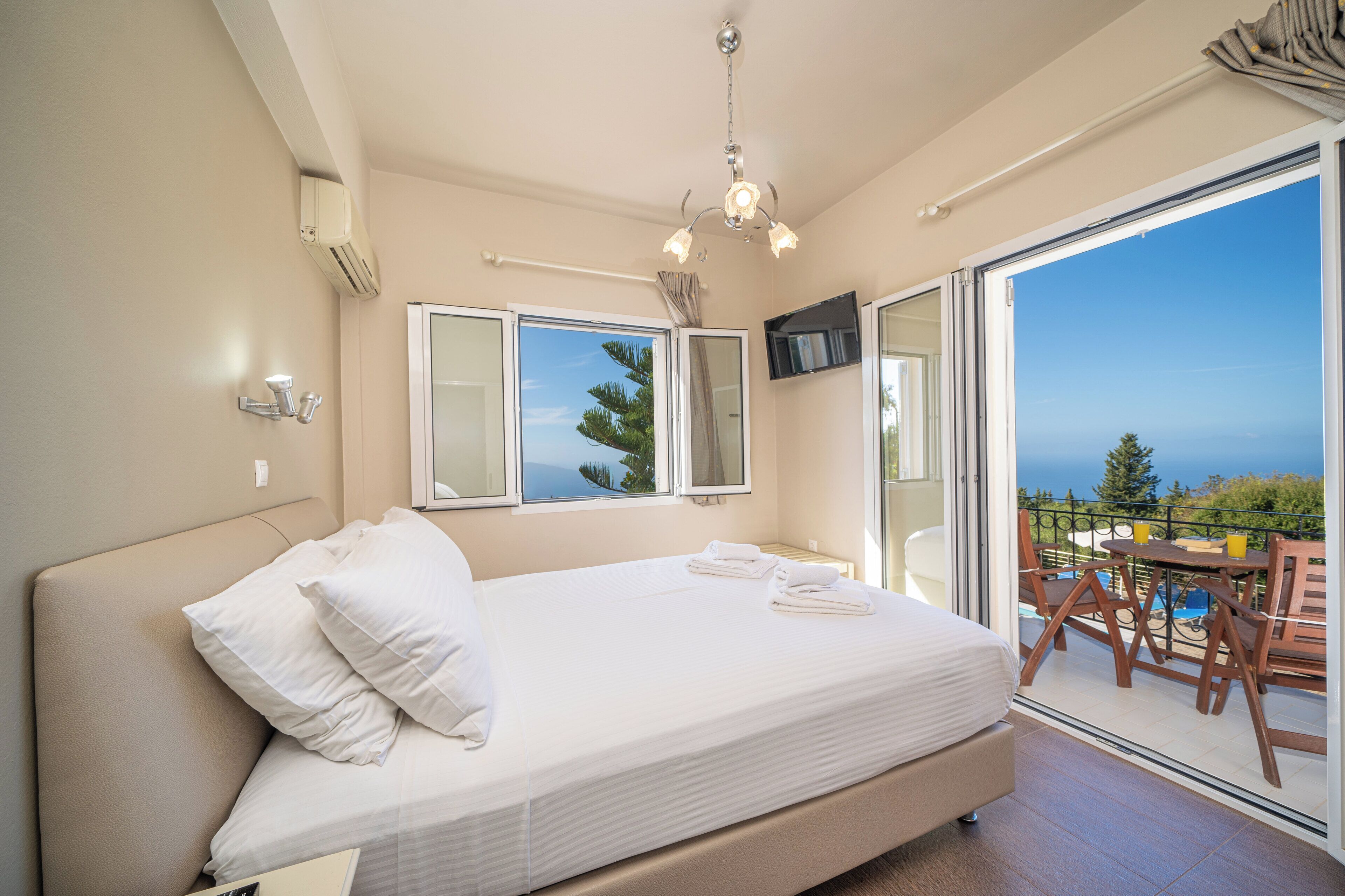 Quarto com uma cama grande, um ventilador de teto e vista para o exterior através de uma porta de correr de vidro.