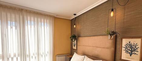 Quarto com uma cama grande, uma mesa de cabeceira com telefone e controle remoto, uma planta pendente e um quadro na parede.