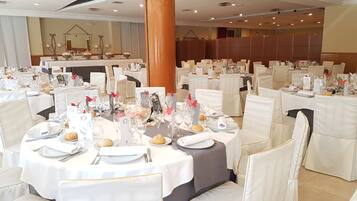 Uma sala de banquetes com mesas redondas, toalhas brancas e cadeiras com capas brancas.