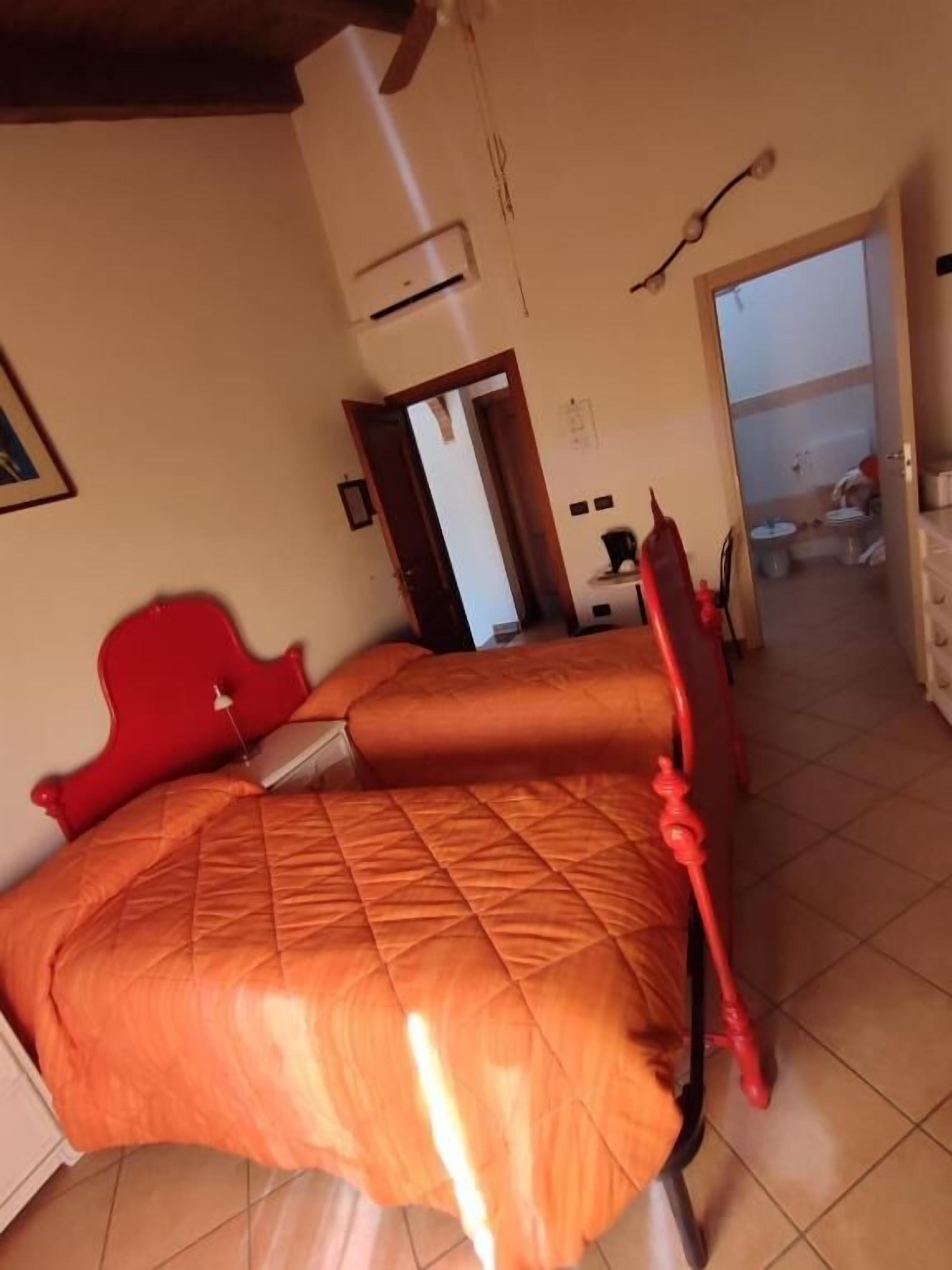 Quarto com cama, cabeceira vermelha, porta e janela.