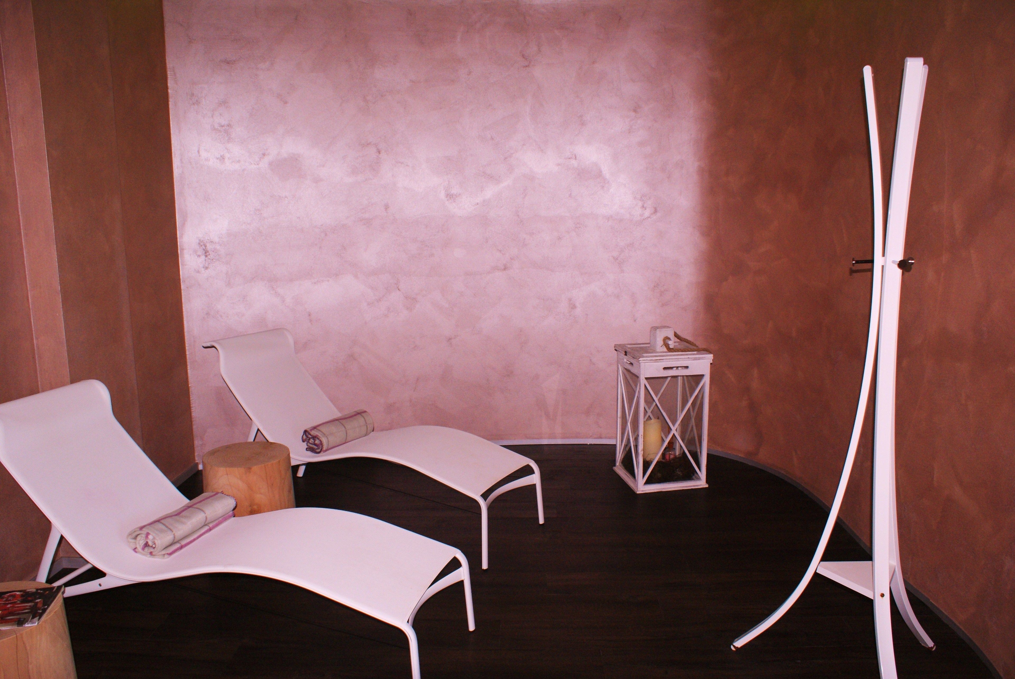 Um quarto com duas poltronas brancas, um banquinho de madeira e um candeeiro branco sobre um chão de madeira escura.