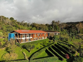 Um edifício moderno com telhado vermelho, rodeado por vegetação exuberante e jardins em terraços.