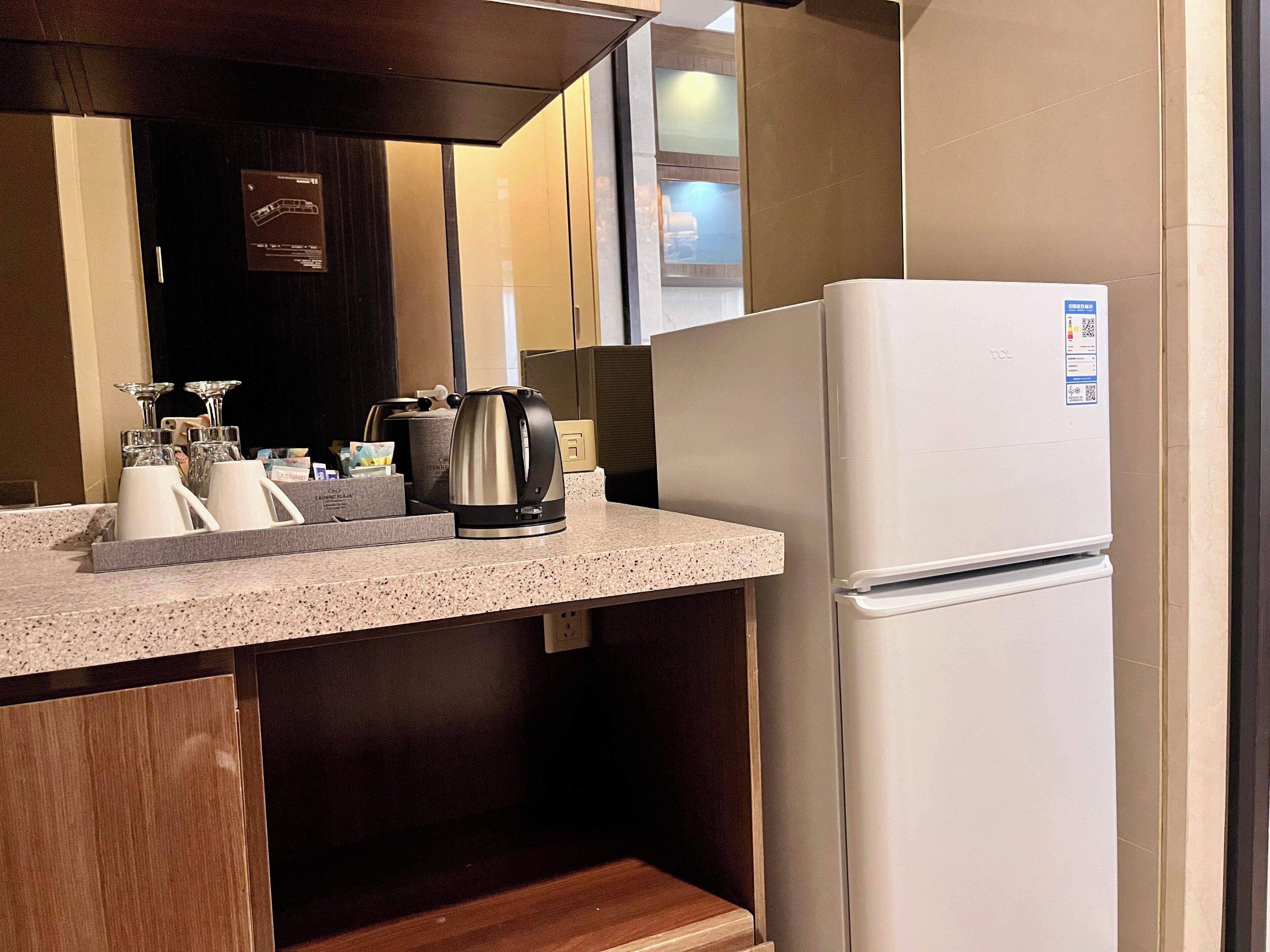Uma cozinha compacta com uma geladeira branca, uma cafeteira e uma chaleira no balcão.