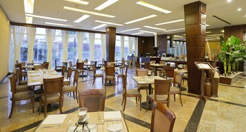Um restaurante amplo com várias mesas e cadeiras, janelas grandes e um pilar central.