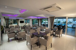 Um espaço de refeições de hotel com várias mesas e cadeiras, janelas amplas e vista para a área da piscina.