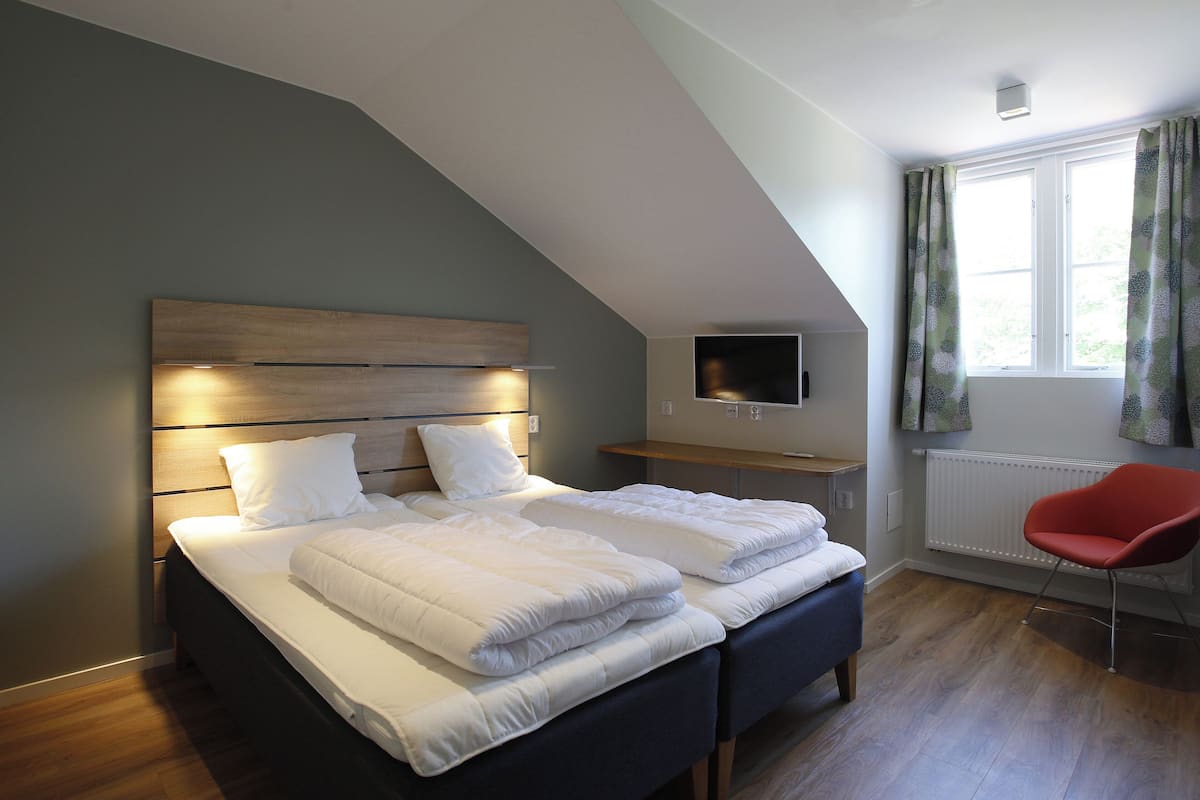 Um quarto com teto estilo loft, uma cama com roupa de cama branca, uma cadeira vermelha e uma televisão em um suporte.