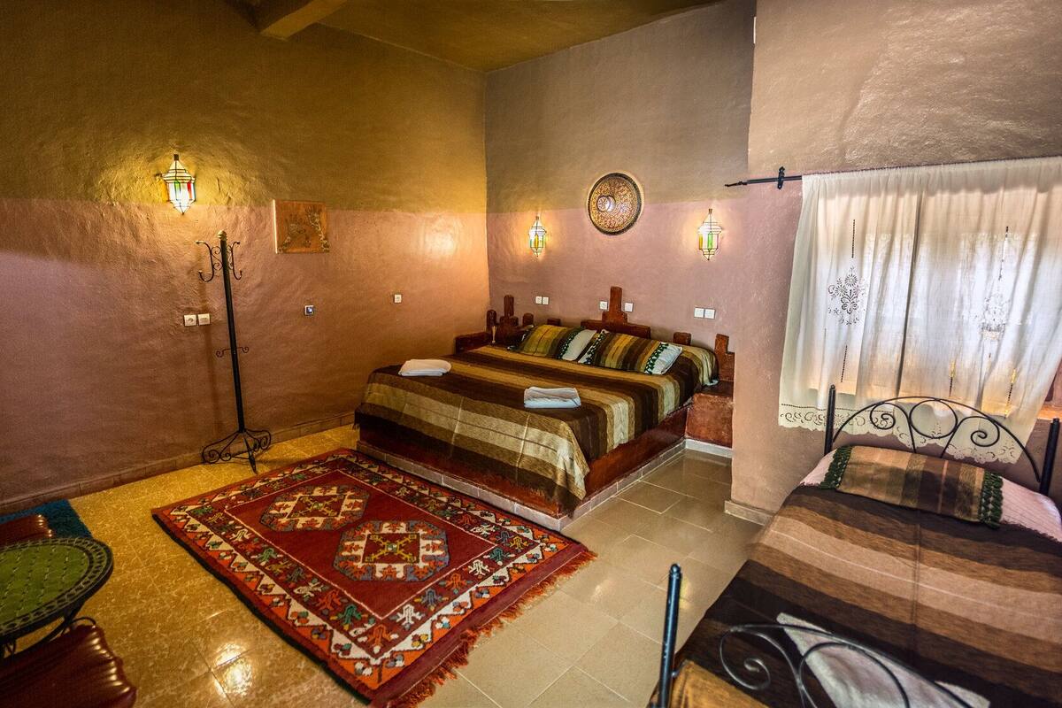 Quarto com duas camas, tapete estampado, luminária de pé e um objeto decorativo na parede.