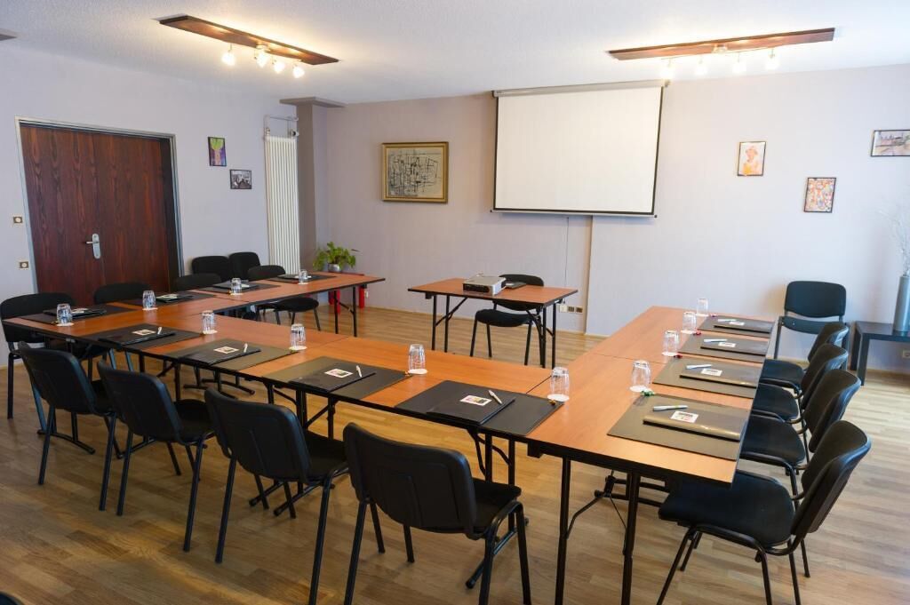Uma sala de conferência com uma mesa comprida, cadeiras pretas, uma tela de projetor e um quadro branco.