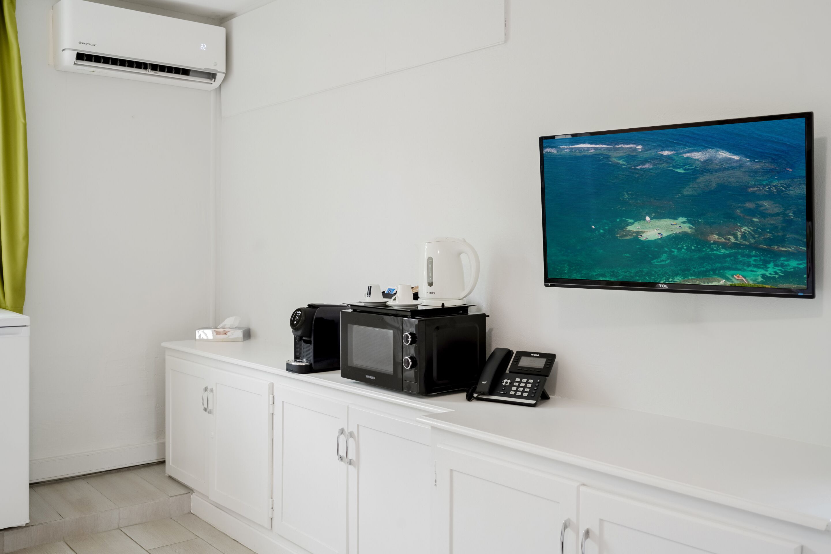 Quarto de hotel moderno com um armário branco, máquina de café, micro-ondas, telefone e televisão exibindo uma vista panorâmica.