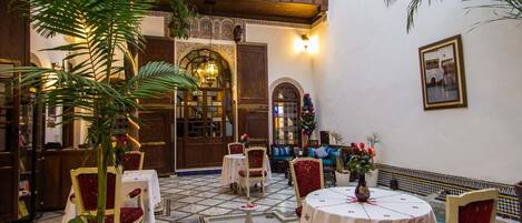 Um interior tradicional com soalho em mosaico, mobiliário de madeira e plantas decorativas.