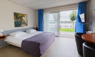 Quarto de hotel com cama, escrivaninha, cadeira, televisão e um quadro.