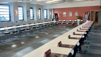 Sala de conferência com mesas compridas, cadeiras e uma parede de destaque vermelha.