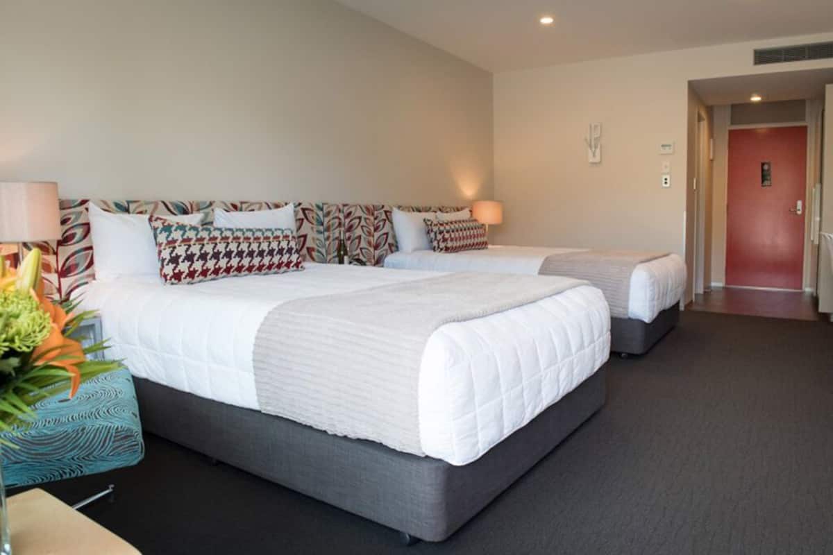 Quarto de hotel com duas camas, uma mesa de cabeceira com abajur e um vaso com planta.