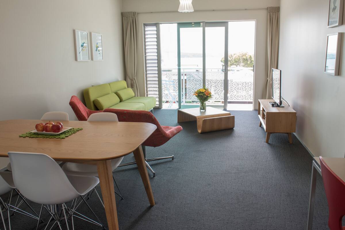 Sala moderna com área de jantar, um sofá verde, televisão e varanda com vista.