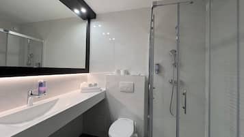 Uma casa de banho moderna com cabine de duche em vidro, lavatório branco e sanita.