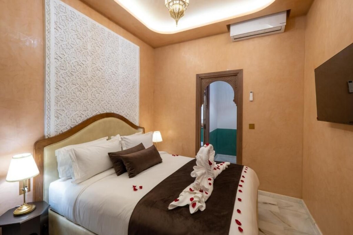 Quarto de hotel com cama, mesa de cabeceira, ar condicionado fixado na parede e porta com design em arco.