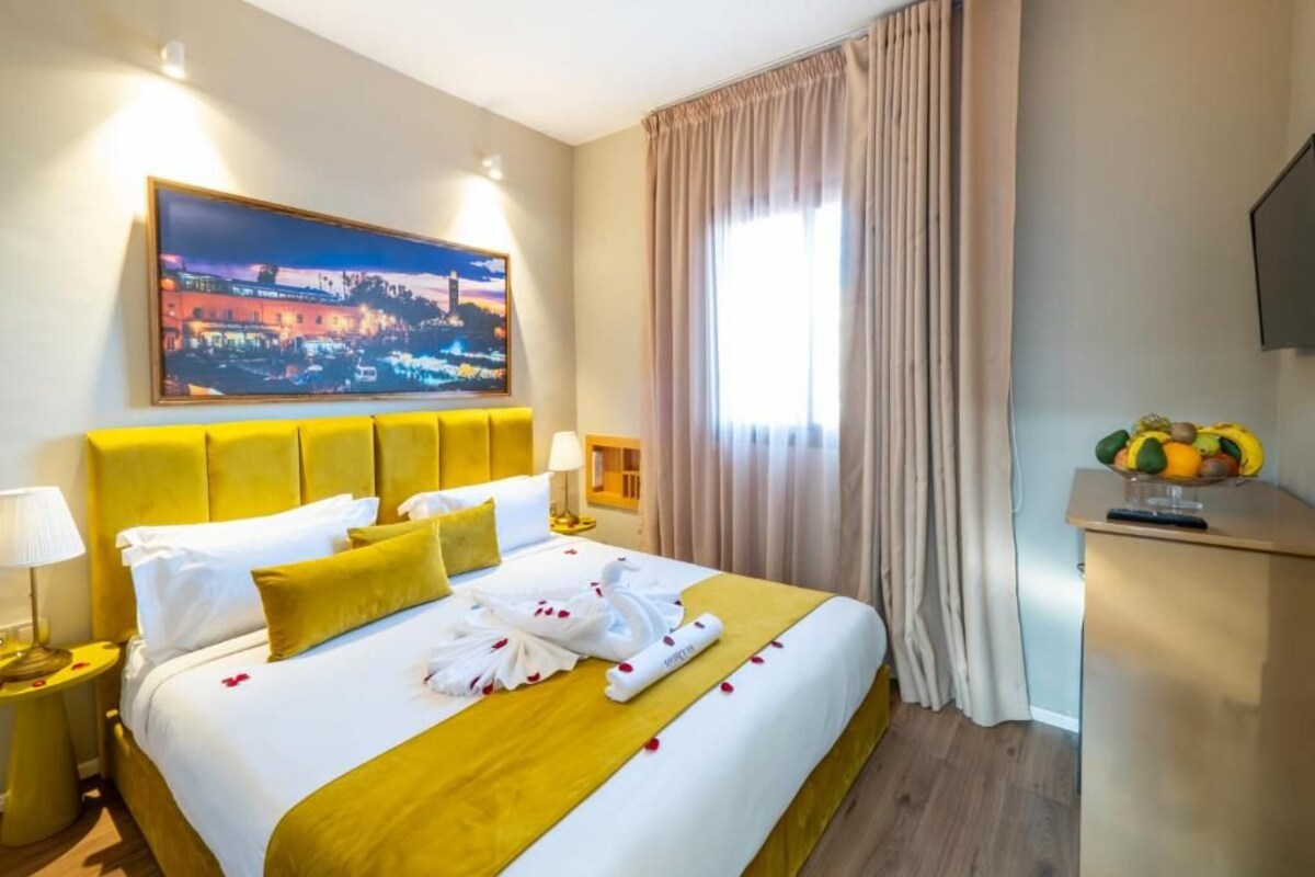 Quarto de hotel com cama, pintura, escrivaninha e cortinas.