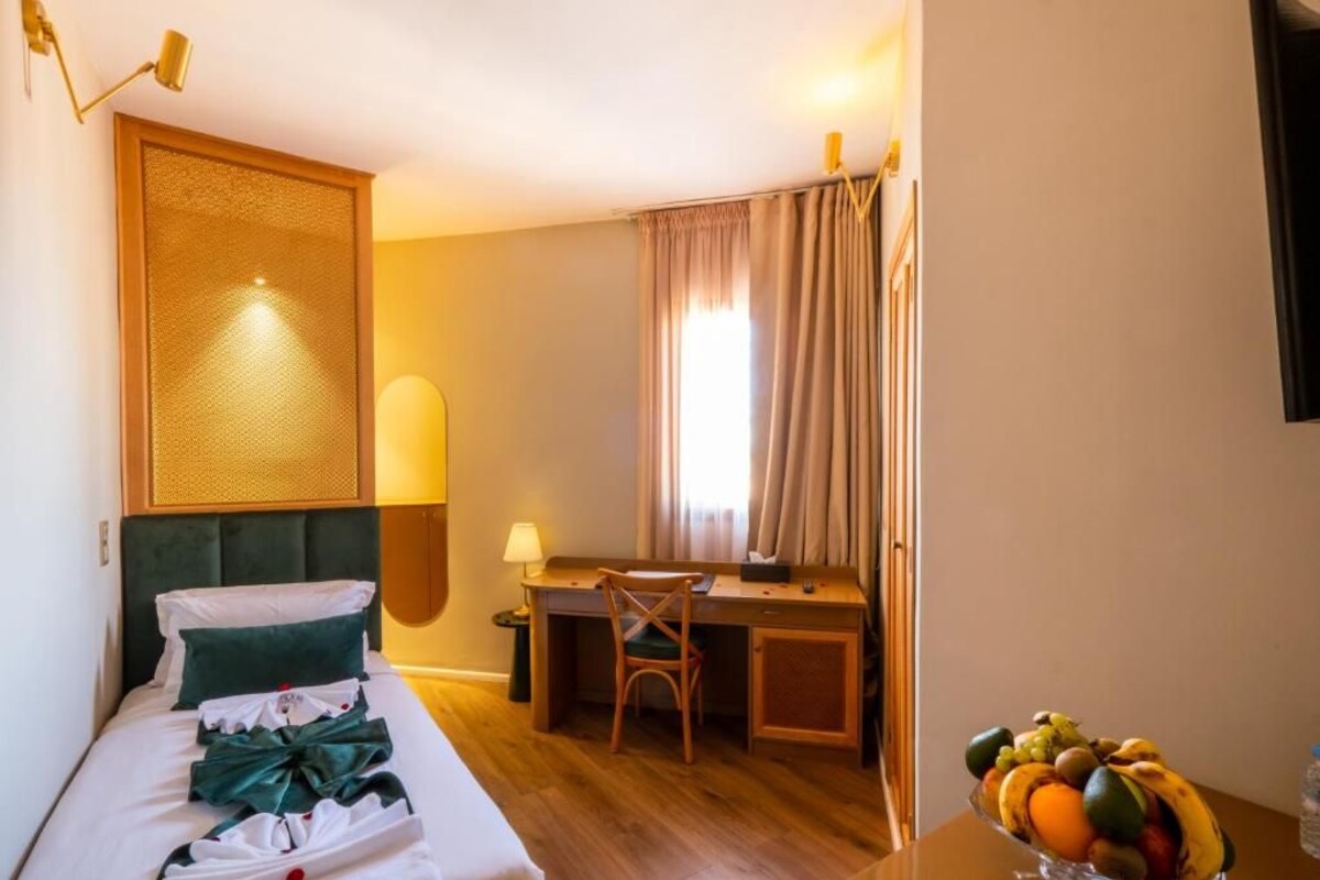 Quarto de hotel com cama, escrivaninha, cadeira e uma cesta de frutas.