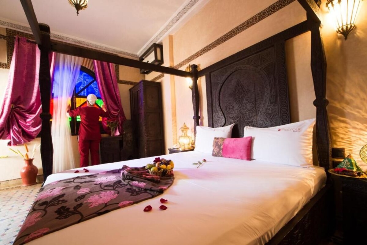 Quarto de hotel com cama grande, mesa de cabeceira, cabeceira decorativa e vista para uma pessoa lá fora.