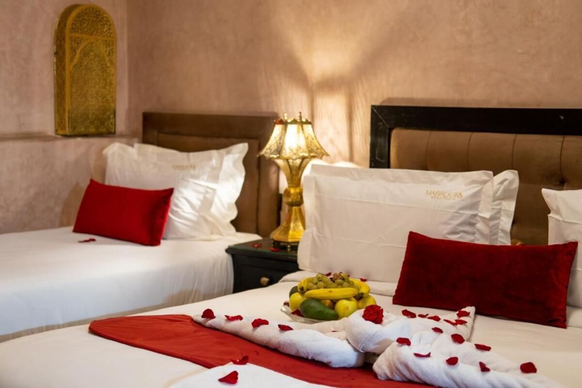 Quarto de hotel com duas camas, mesa de cabeceira, abajur e um objeto decorativo na parede.