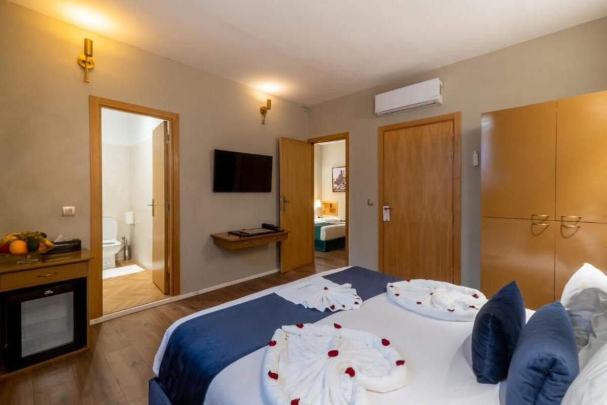 Quarto de hotel com cama, mesas de cabeceira, guarda-roupa e televisão.