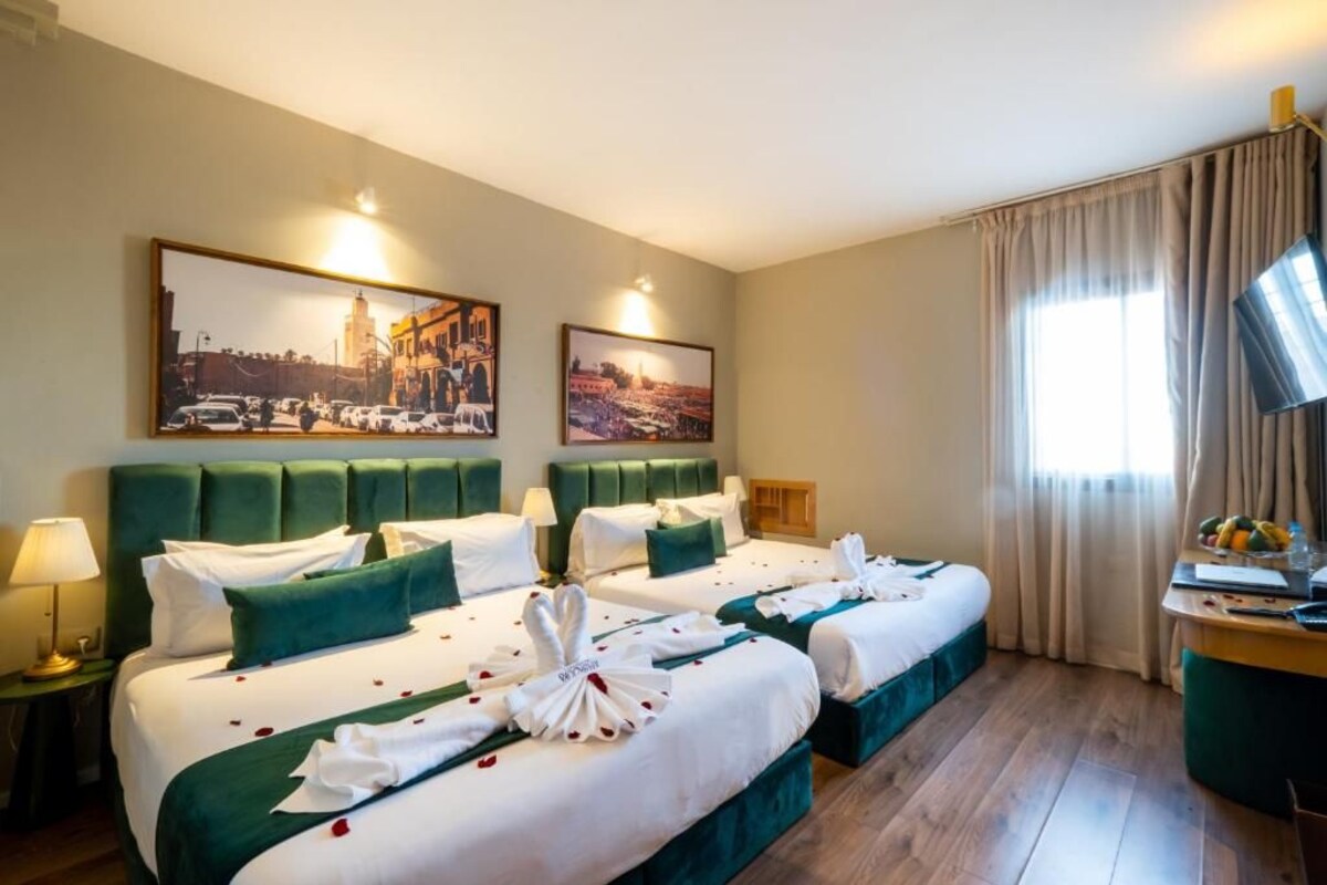 Quarto de hotel com duas camas, televisão, escrivaninha com cadeira e janela com cortinas.