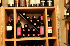 Uma estante de madeira com várias garrafas de vinho, incluindo marcas como Mazzolada e Ceccai.
