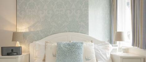 Uma cama bem arrumada com um travesseiro fofo, uma luminária de cabeceira e uma mesinha de apoio com um rádio.