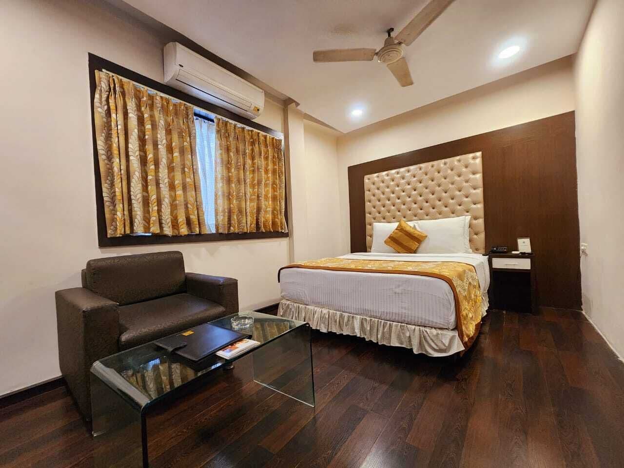 Quarto de hotel com cama, sofá, mesa de centro de vidro e ar condicionado.