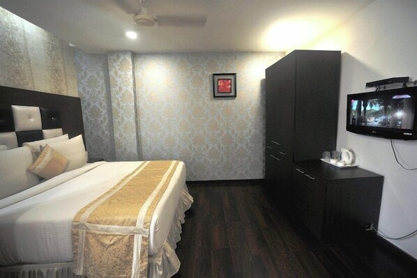 Quarto de hotel com cama grande, guarda-roupa, televisão e uma pequena mesa com chaleira.