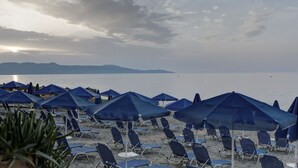 Uma praia com fileiras de guarda-sóis azuis e espreguiçadeiras.