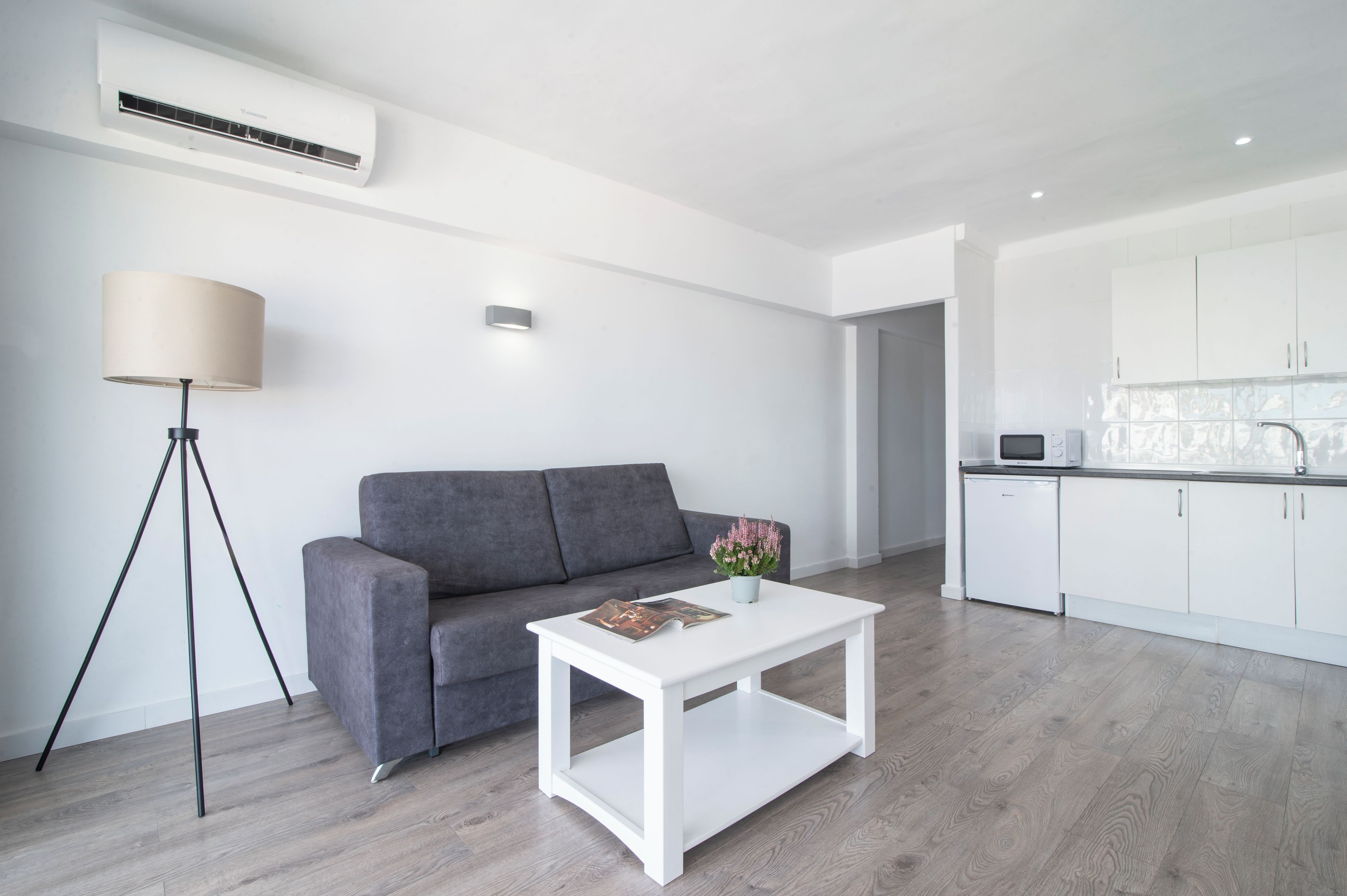 Uma sala de estar moderna com um sofá cinzento, uma mesa de centro branca e um abajur.