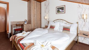 Cama bem arrumada com travesseiros e cobertor, escrivaninha de madeira com cadeira e um quadro na parede.