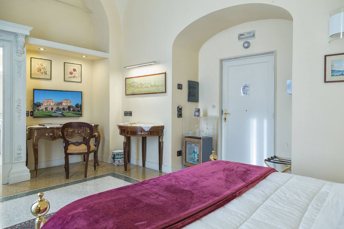 Quarto de hotel com cama, escrivaninha, cadeira, mesinha e porta.