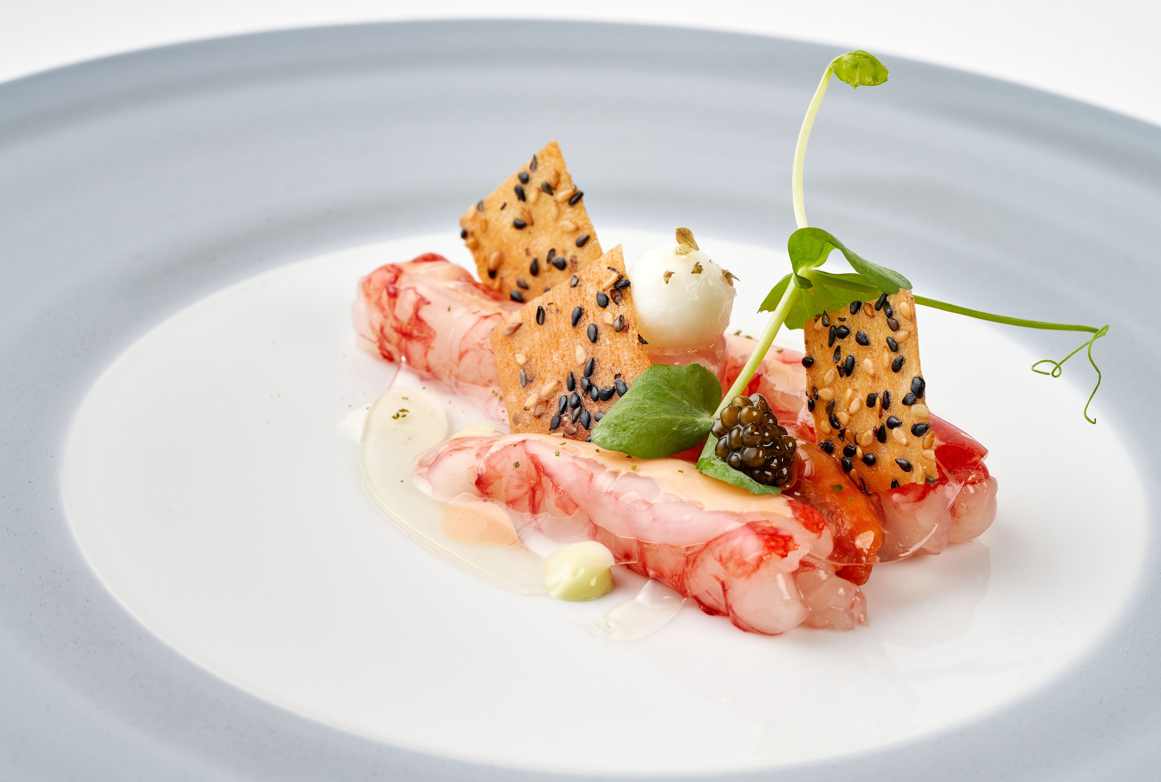 Um prato com uma porção de sashimi, decorado com sementes de gergelim, uma folha verde pequena e um broto.