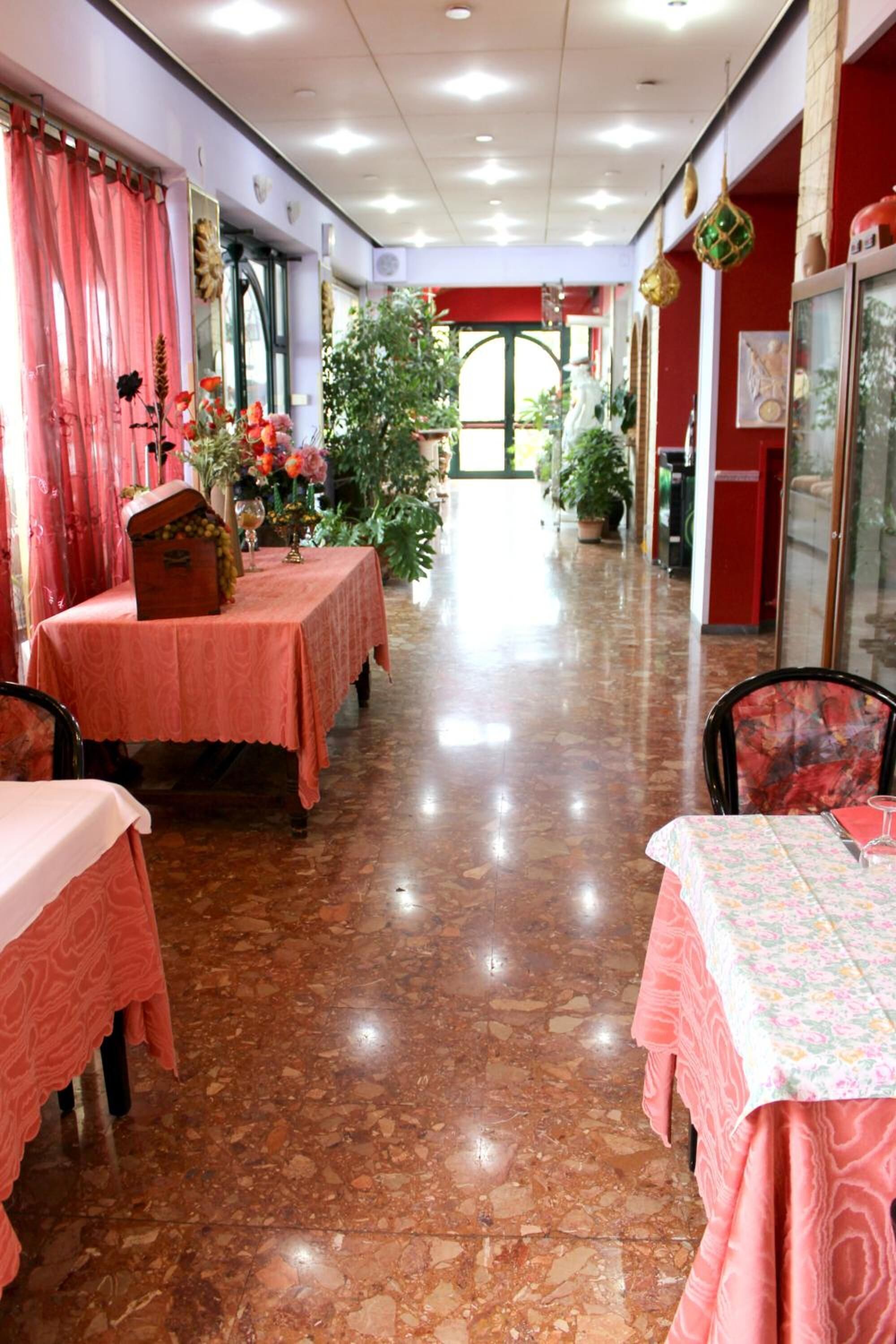 Um hall de hotel com piso de mármore polido, cortinas vermelhas e mesas decoradas com toalhas de mesa florais.