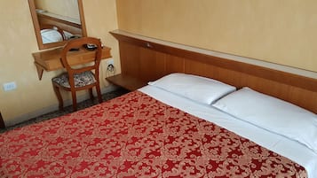 Quarto de hotel com uma cama, uma escrivaninha com cadeira e um espelho.