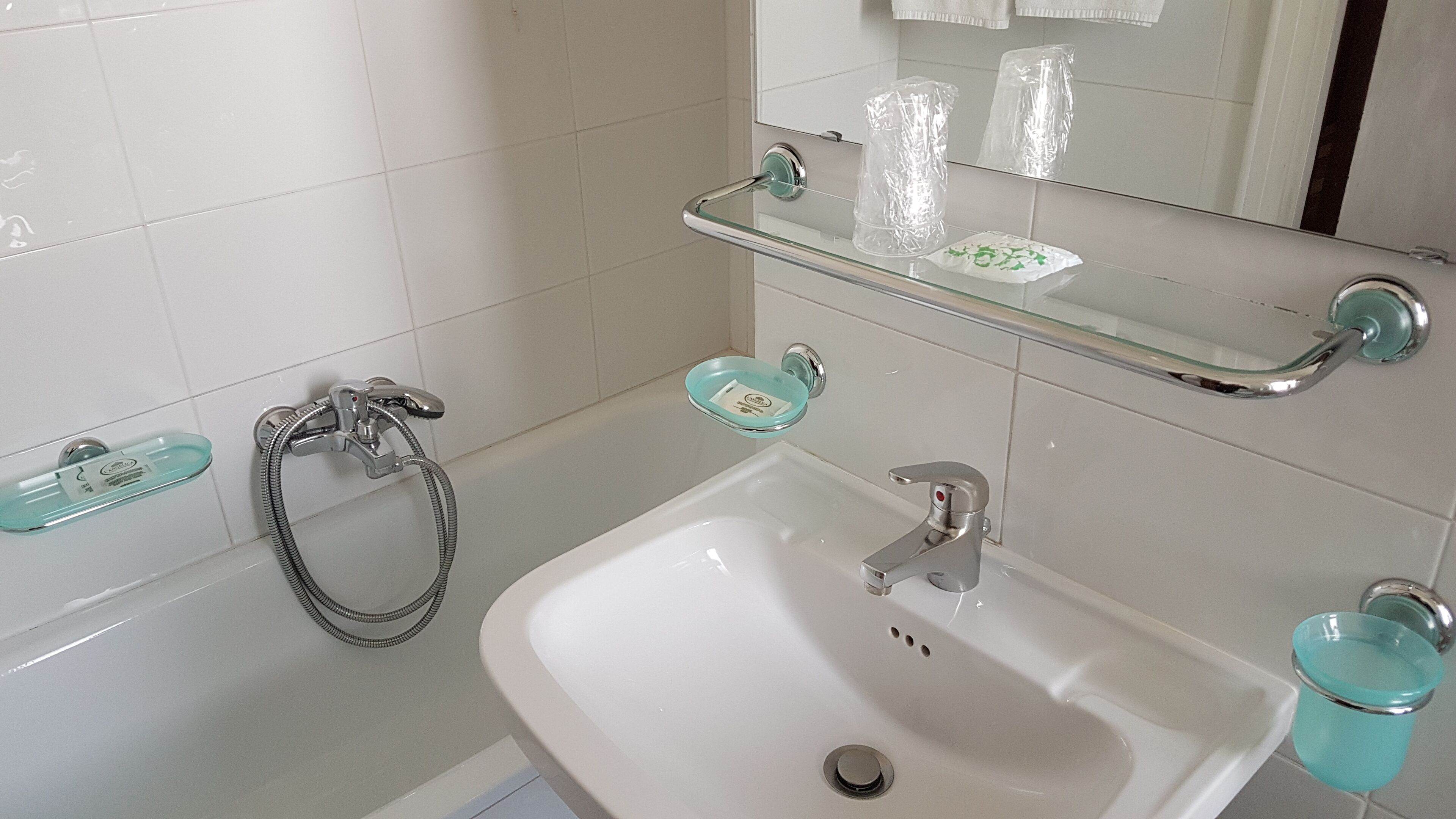 Casa de banho com lavatório branco, cabine de duche em vidro e prateleira de vidro com produtos de higiene pessoal.