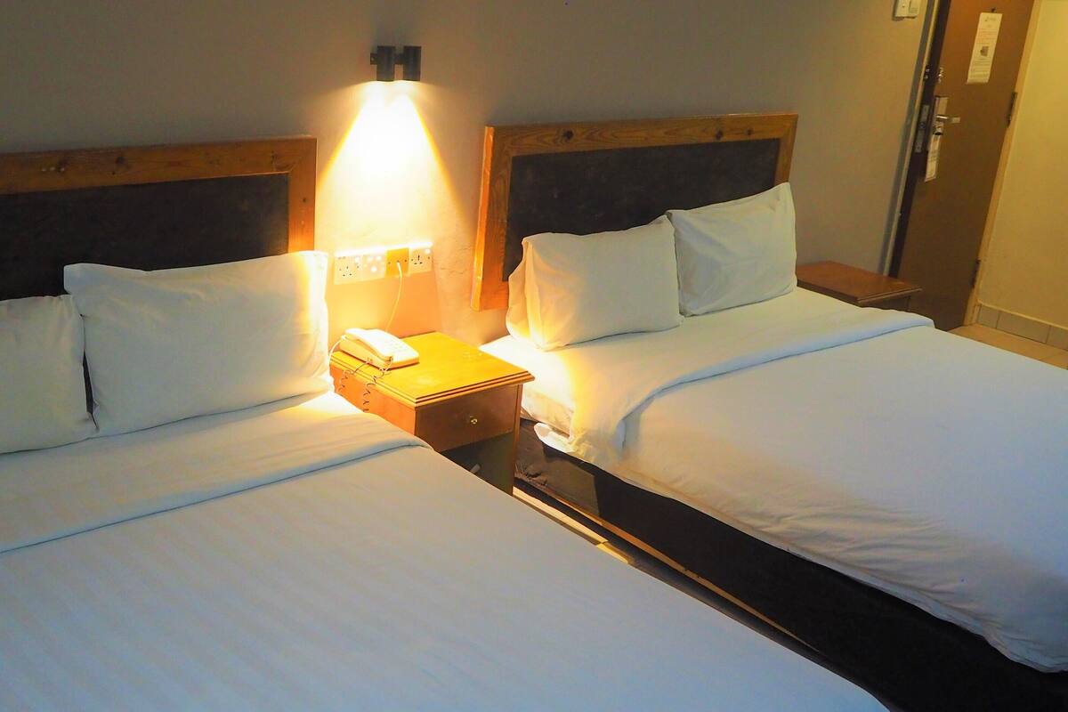 Duas camas de solteiro com cabeceiras de madeira, roupa de cama branca e abajures.