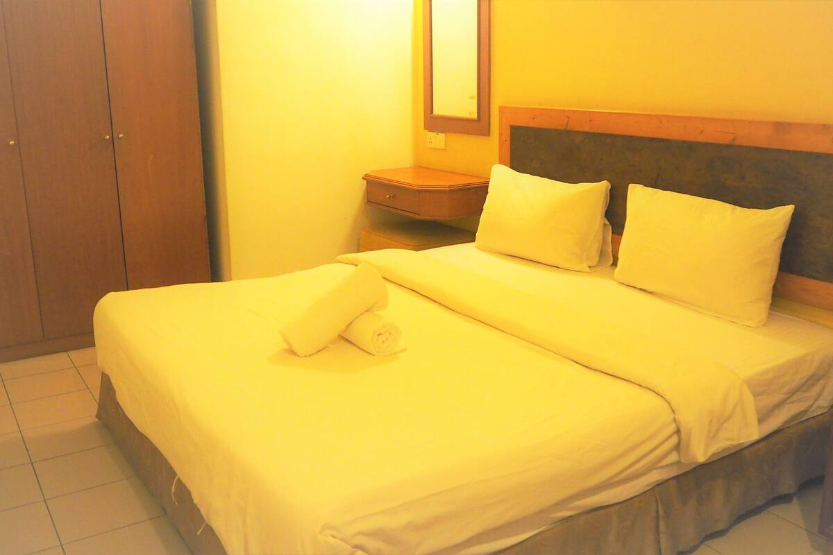 Quarto de hotel com uma cama, cabeceira de madeira, mesa de cabeceira e espelho na parede.