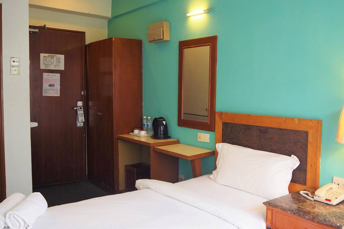Quarto de hotel com cama, mesa de cabeceira, luminária e espelho.