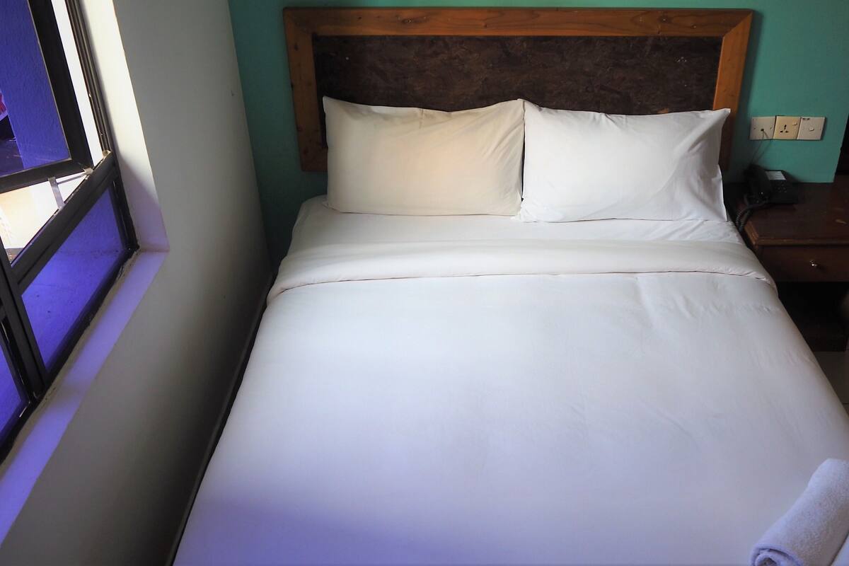 Uma cama bem arrumada com lençóis brancos, uma cabeceira de madeira e uma mesa de cabeceira com um telefone.