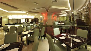 Uma sala de jantar moderna com divisórias de vidro, cadeiras estofadas verdes e mesas bem arrumadas.