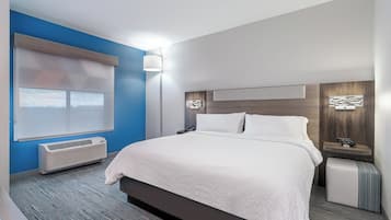 Quarto de hotel moderno com cama grande, janela com persianas, luminária de cabeceira e mesa de cabeceira pequena.