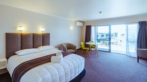 Quarto de hotel com uma cama grande, área de estar com mesa e cadeiras, e vista pela janela.
