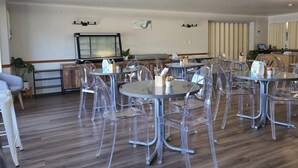 Uma sala de jantar com mesas redondas e cadeiras transparentes, uma televisão e piso de madeira.