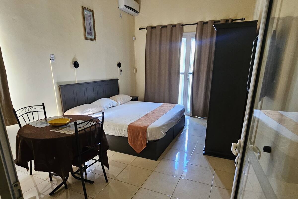 Quarto de hotel com uma cama, uma mesa de jantar, um ventilador de teto e um aparelho de ar condicionado.